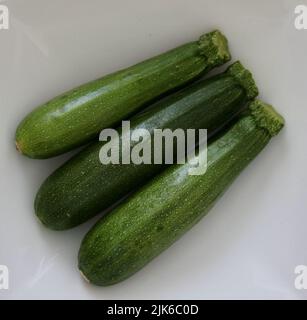 Three assorted green courgettes lying on a plain white background Stock ...