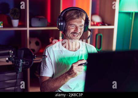 Young blond man streamer playing video game with winner expression at ...