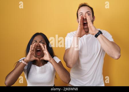 Interracial couple standing over yellow background doing peace symbol ...