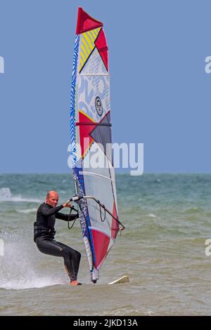 Recreational windsurfer in black wetsuit practising classic windsurfing ...