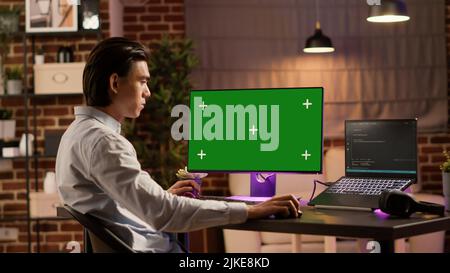 Asian businessman looking at computer with greenscreen on display ...