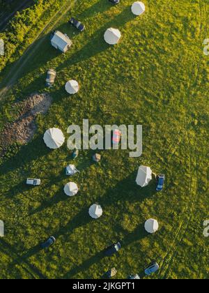 An aerial view of an idyllic campsite with bell tents and cars in a ...