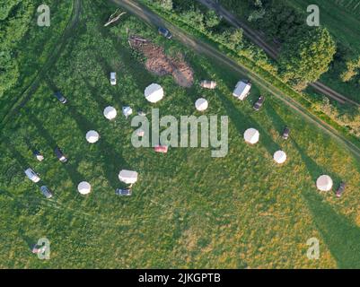 An aerial view of an idyllic campsite with bell tents and cars in a ...