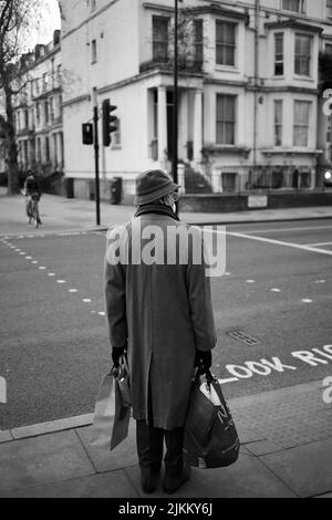 A grayscale shot of a man standing on the rocky shore fishing in the ...