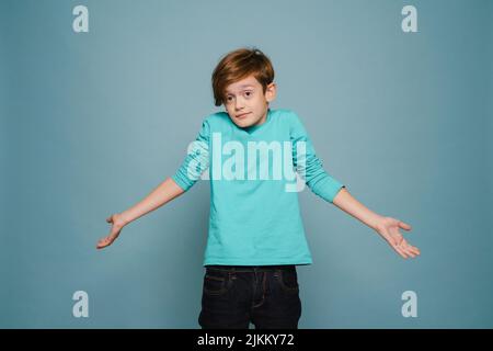 Ginger perplexed boy gesturing and looking at camera isolated over blue ...