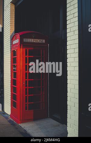 A vertical shot of the red phone booth in a park in London on ana ...