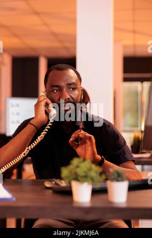 Employee talking at landline phone with remote supervisor, working at ...