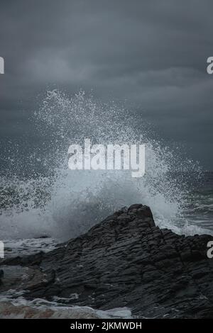A vertical shot of a sea storm with splashing waves and rocks under a ...