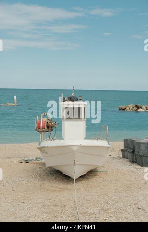A vertical shot of a small boat on the beach with sea and cloudy blue ...