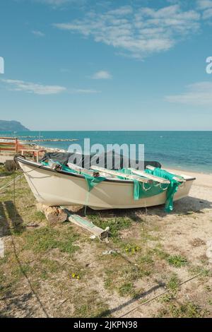 A vertical shot of a small boat on the beach with sea and cloudy blue ...