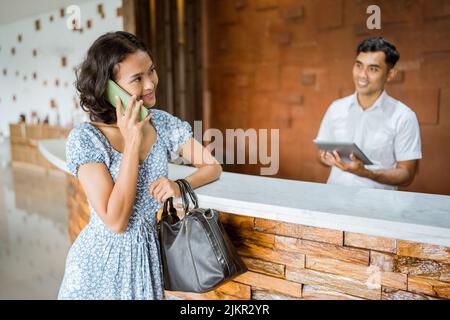 Female guest calling with smartphone at reception in hotel lobby Stock ...