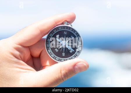 Closeup, hand holding an analog compass in front of the sea, summer ...