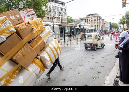 A teenager worker dragging large hand-pulled cart with wrapped boxes ...