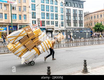 A teenager worker dragging large hand-pulled cart with wrapped boxes ...