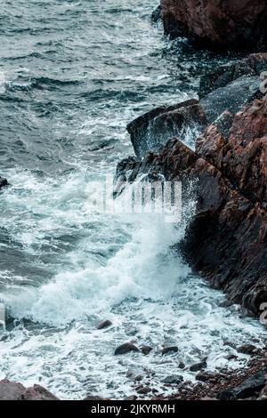 A vertical shot of splashing foamy waves on a cliff Stock Photo - Alamy