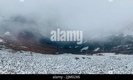 A scenic view of a rocky mountain enveloped in white clouds in a rural ...
