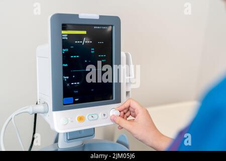 Doctor operating vital sign monitor in patient room of modern hospital ...