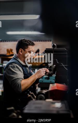 A male locksmith wearing glasses making a key in front of an equipment ...