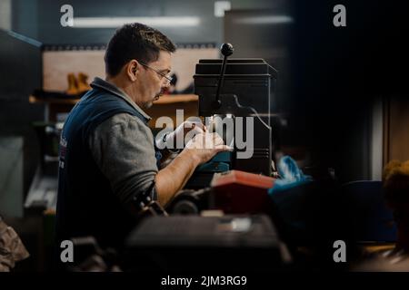 A male locksmith wearing glasses making a key in front of an equipment ...