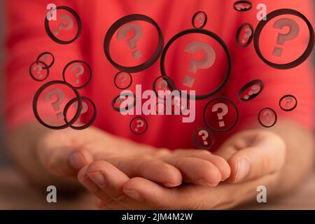 A person's hand with illustrative question mark icons floating above ...