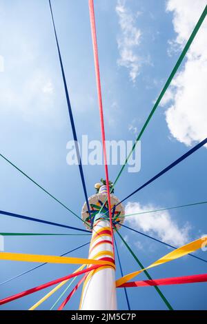 A vertical shot of a pole with colored ribbons and flowers on a ...