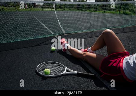 A faceless girl in a sports skirt sits on a tennis court and holds a ...