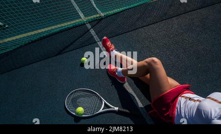 A faceless girl in a sports skirt sits on a tennis court and holds a ...