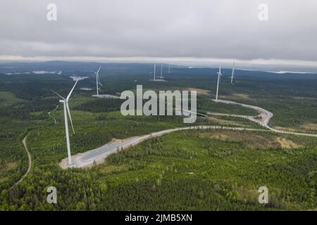 The wind turbines surrounded by dense green trees against a cloudy sky ...