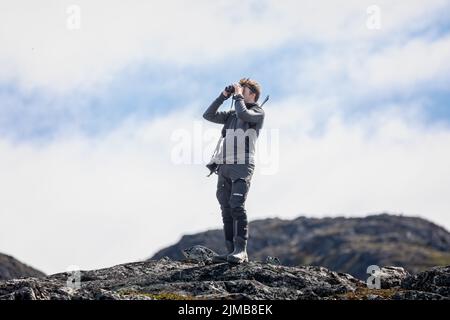 Male lookout armed with rifle scanning for polar bears in the tundra at ...