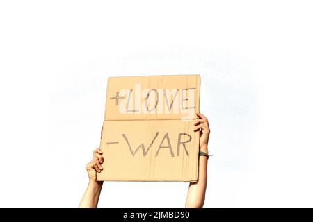 A cardboard sign saying more love, less war, and stop war held by two ...