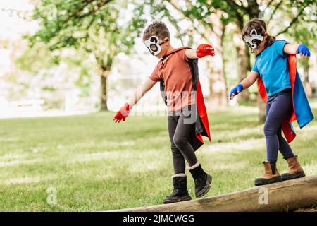 Brother and sister in superhero capes and animal masks hiding behind ...