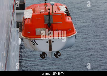 Lowering orange totally enclosed lifeboat to water. Abandon ship drill ...