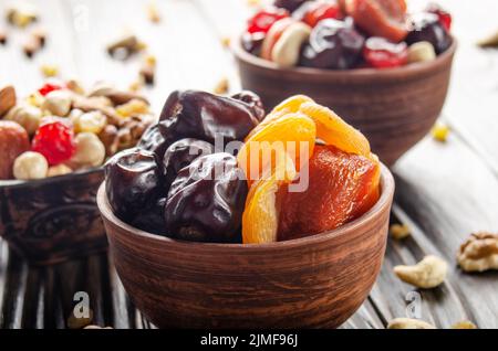 Dried dates and apricots in clay bowl on wooden kitchen table closeup ...