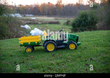 Child's toy riding tractor in green grass yard with farm background ...