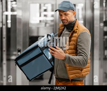Handsome delivery man with box and mobile phone on white background ...
