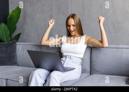 Overjoyed young woman sit on couch at home triumph receive pleasant ...