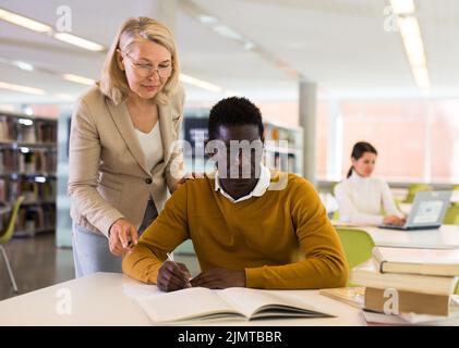 Friendly female tutor helping to diligent african-american man ...