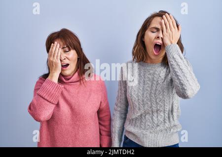 Hispanic mother and daughter together yawning tired covering half face ...