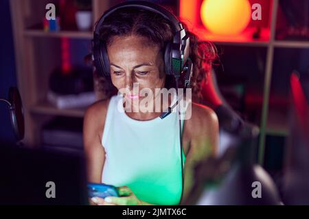Middle age woman streamer using computer and smartphone at gaming room ...