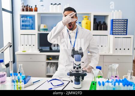 Hispanic man working as scientist peeking in shock covering face and ...