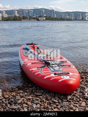 Red SUP board on the river bank. Paddle board on the lake shore ...