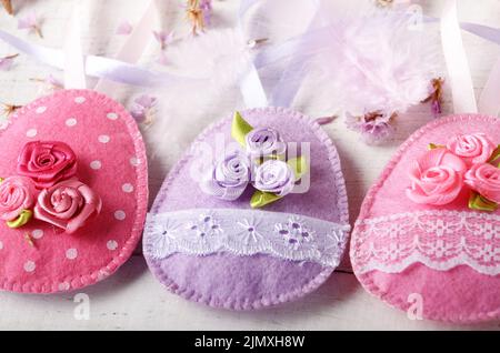 Handmade patchwork pink and lilac felt easter eggs on white wooden ...