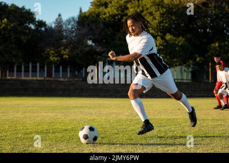 Biracial male player with dreadlocks running and kicking ball during ...