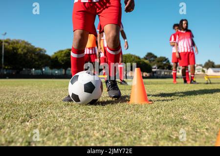 Low section of male multiracial players dribbling ball between cones at ...