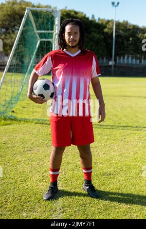 Portrait of biracial male player with dreadlocks holding soccer ball ...