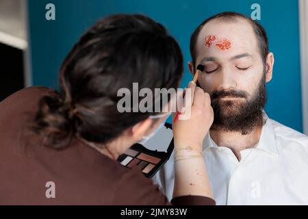 Artist using makeup and costume to create zombie look, sitting in ...