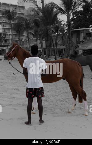 A grayscale shot of a man standing on the rocky shore fishing in the ...