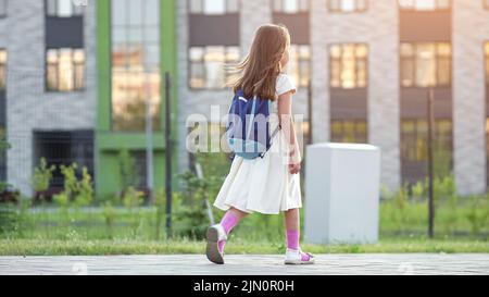 Preschooler girl with schoolbag walks past school building Stock Photo ...