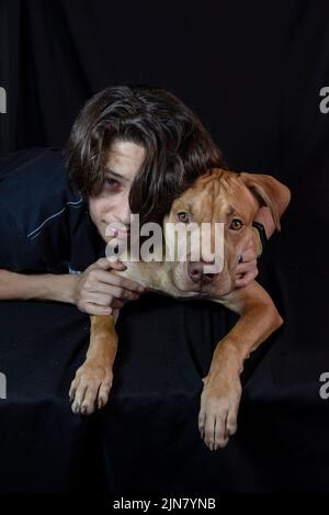 Portrait of a young man with a caramel colored pitbull dog against ...