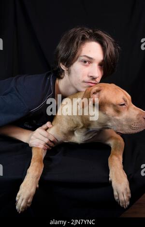 Portrait of a young man with a caramel colored pitbull dog against ...